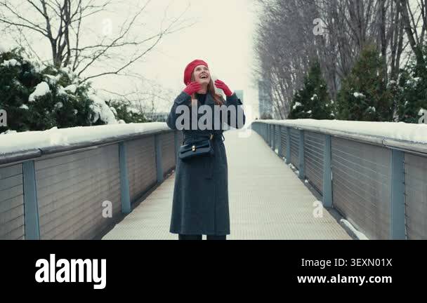 A beautiful girl wearing a gray coat, a red hat, and red gloves walks ...