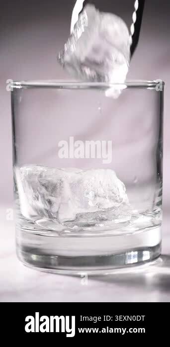 Vertical close-up video of adding ice cubes with tongs into a ...