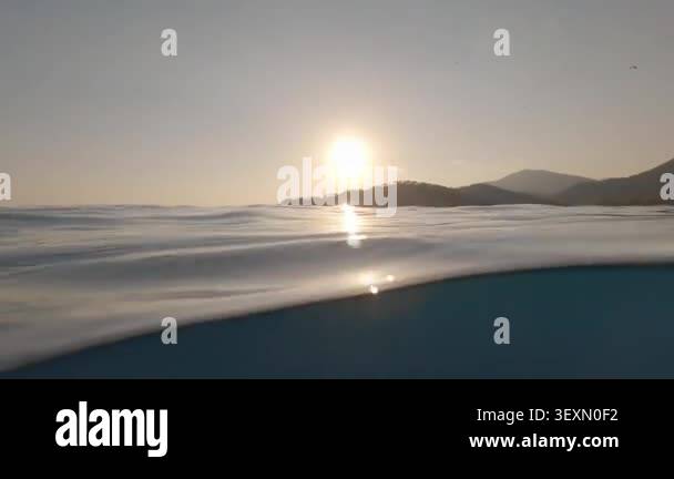 Swimming at sea during sunset, sun setting down behind hills in ...