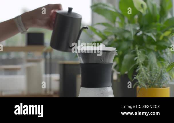 Hand pours water from kettle into paper filter set in coffee dripper on ...