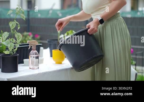Woman fills yellow flower pot with soil from bucket using scoop at ...