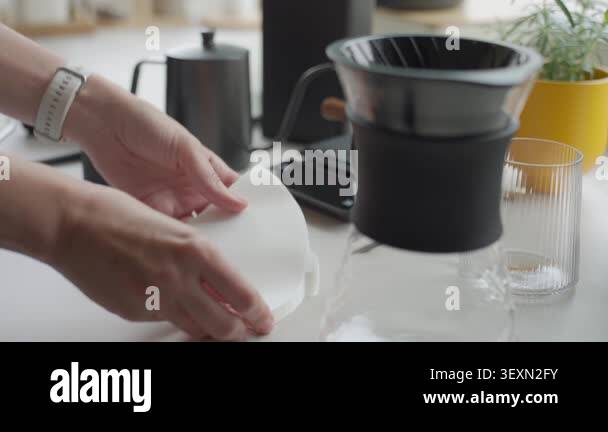 Hands preparing paper filter for pour over coffee beside dripper and ...