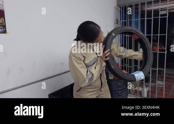 Female mechanic in a beige jumpsuit inspecting a new motorcycle tire in ...