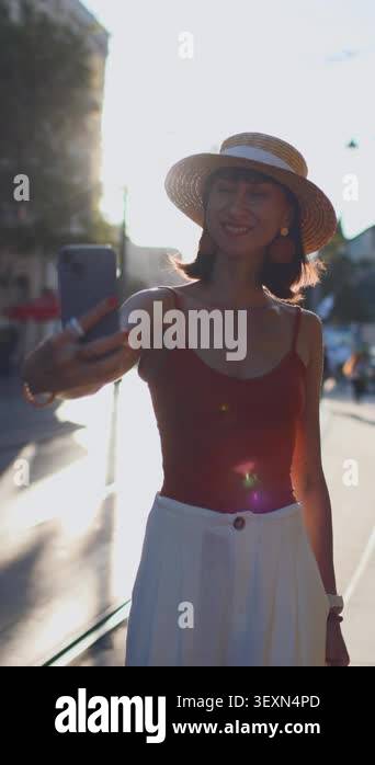 vertical video. A woman is taking a selfie on her smartphone using a ...