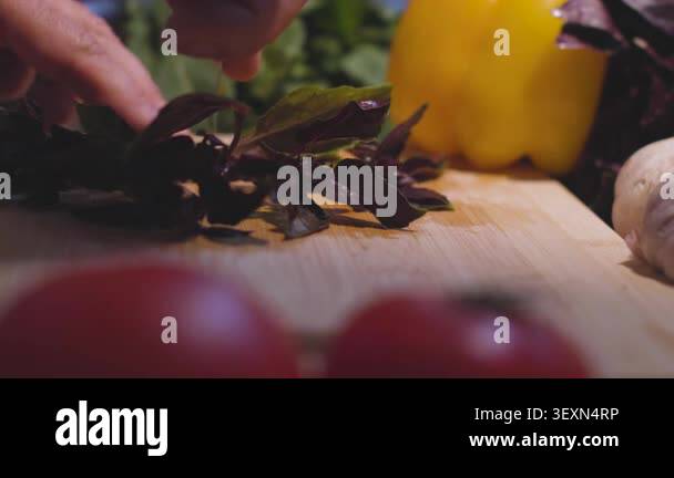 A mans hand chops fresh basil for a salad on a wooden cutting board ...