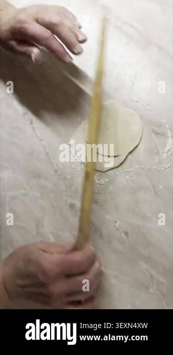 High angle view of hands using a thin wooden pin to roll small circles ...