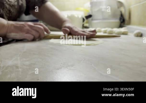 Close up shot of hands using a thin wooden pin to roll pieces of dough ...