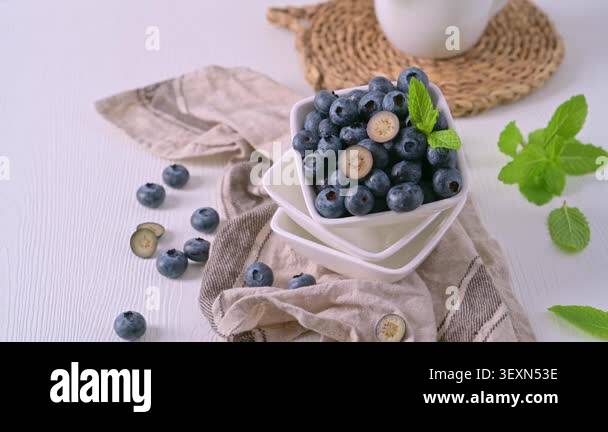 A white square bowl filled with plump blueberries sits on a rustic ...