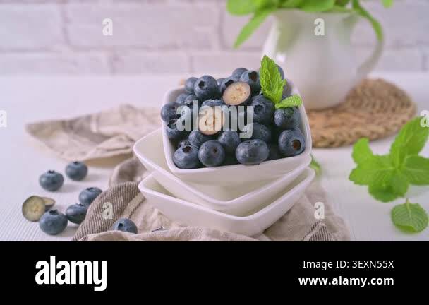 A white square bowl filled with plump blueberries sits on a rustic ...