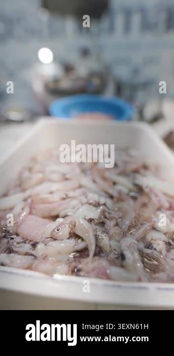Close-up of a white tray filled with small, fresh squid for sale at a ...