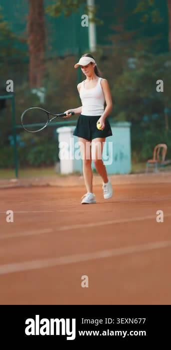 Young woman tennis player in white tank top and black skirt gets ready ...