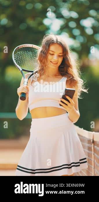 Young female tennis player checks her smartphone while holding a racket ...