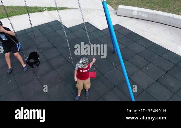 Aerial view of two children swinging on a playground, one in a red ...