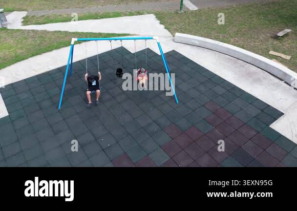 Aerial view of two people swinging on a playground swing set, one ...