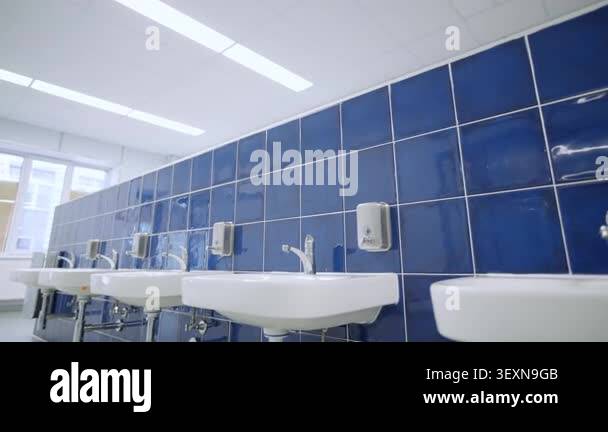 Spacious washroom displays orderly line of washbasins with glossy tiles ...