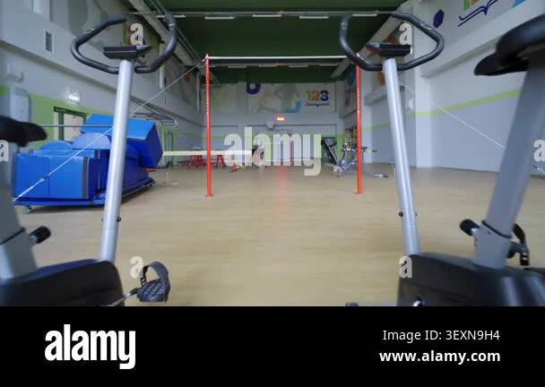 Stationary bikes stand in gymnasium with gymnastics equipment. Bright ...