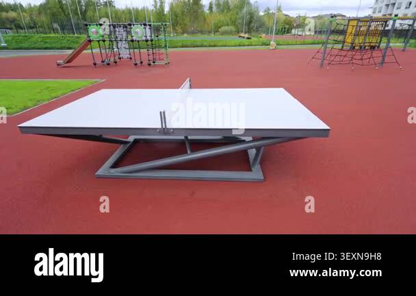 Ping pong table stands on red rubber playground surface. Various ...