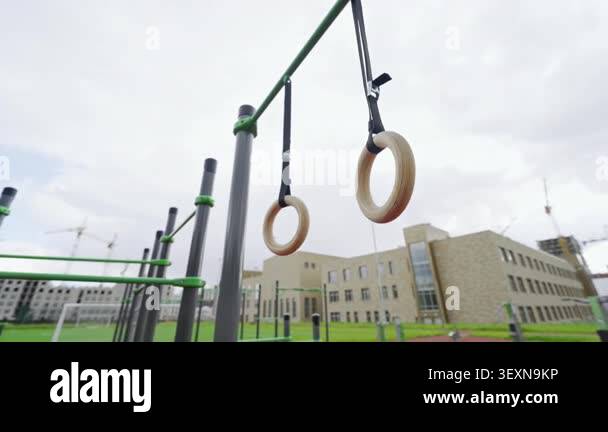Wooden gymnastic rings hang from metal bar at outdoor workout station ...