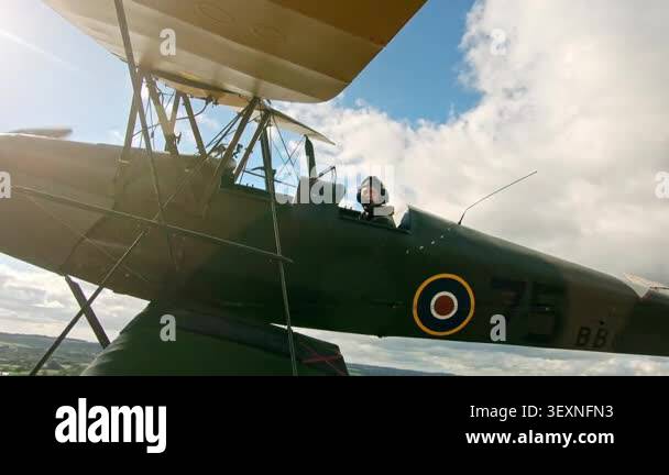 World war two military biplane flying in a cloudy blue sky with the sun ...