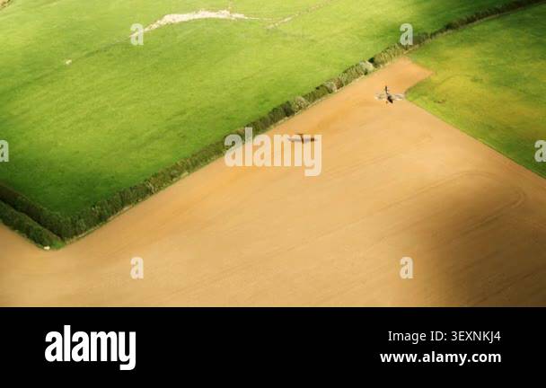 Aerial view of a vintage biplane flying low over agricultural fields in ...