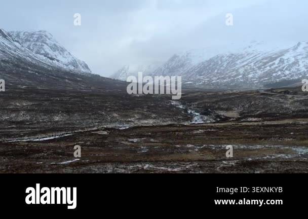 Dramatic, desolate valley with snow capped mountains and a stream on a ...