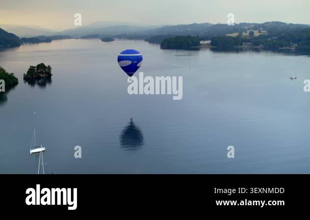 Aerial footage shows a blue hot air balloon flying low over a serene ...