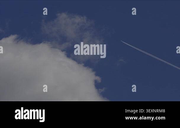 Aviation contrail of an airplane in the blue sky above white fluffy ...