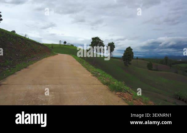 Scenic concrete road winding through green hills under dramatic cloudy ...