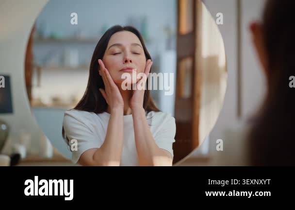 Brunette performing facial massage looking mirror at daily beauty ...