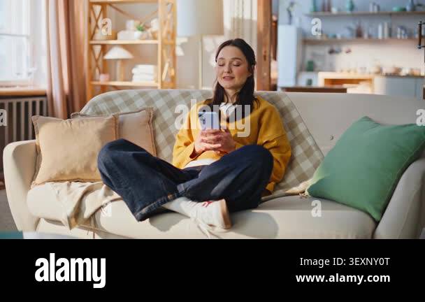 Serene lady using smartphone sitting cozy couch modern apartment ...