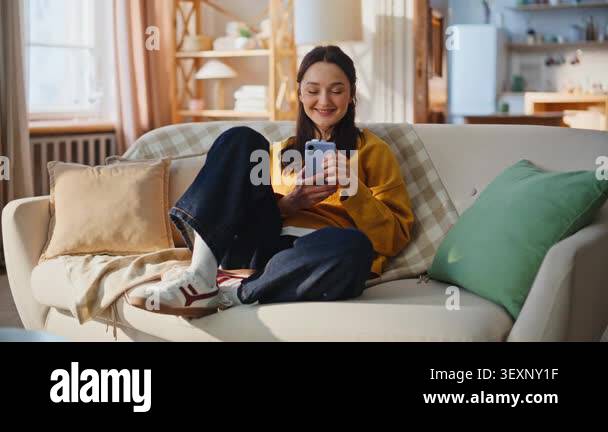 Happy brunette chatting mobile phone resting sofa home. Relaxed ...