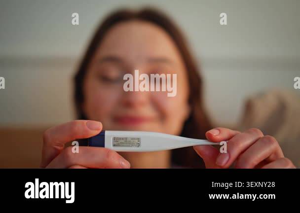 Satisfied lady looking thermometer sitting bed closeup. Smiling woman ...