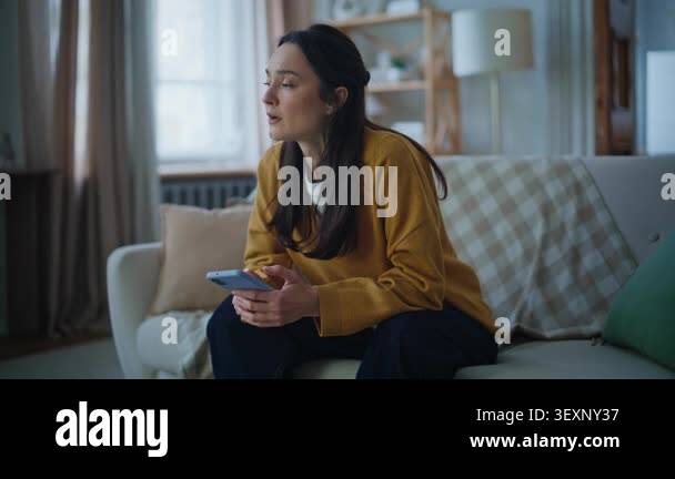 Worried woman browsing cellphone sitting couch home with tense ...