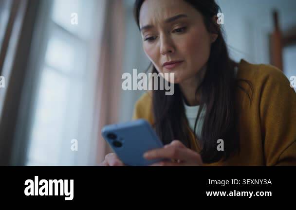Serious brunette looking mobile phone with concerned face sitting couch ...