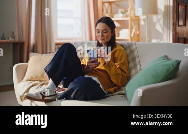 Woman browsing smartphone content sitting comfortably on couch home ...