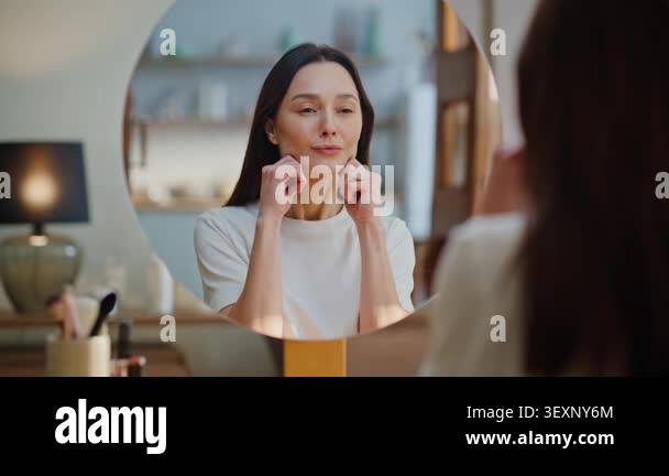 Woman gently massaging face looking home mirror at relaxing skincare ...