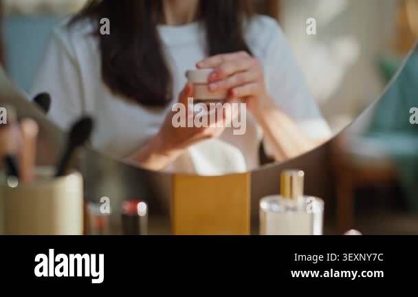 Brunette taking cosmetic moisturizer opening jar in cozy domestic room ...