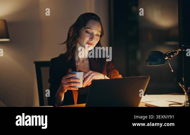 Happy manager holding coffee cup reading computer in dark office ...