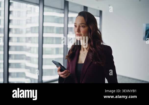 Serious businesswoman looking cellphone walking modern office hall ...