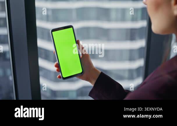 Woman hand touching green screen smartphone at cityscape workplace ...