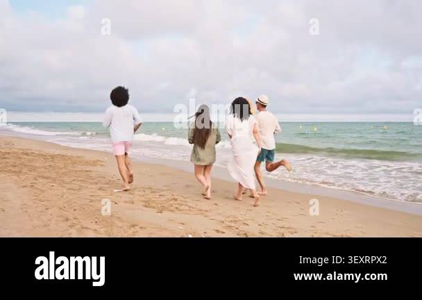 Young diverse group of friends having fun and running barefoot along ...