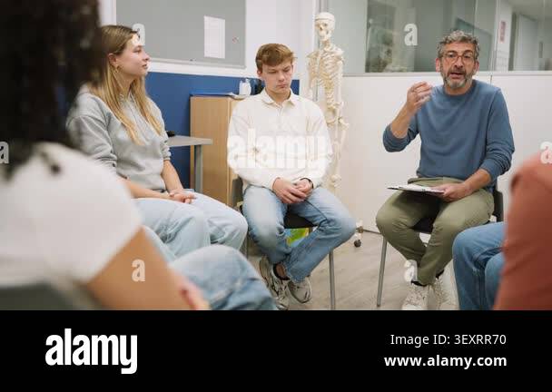 Diverse group of young students and a male professor sitting in a ...