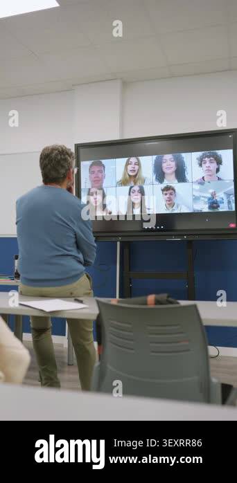 Male professor teaching a class with some students present and others ...