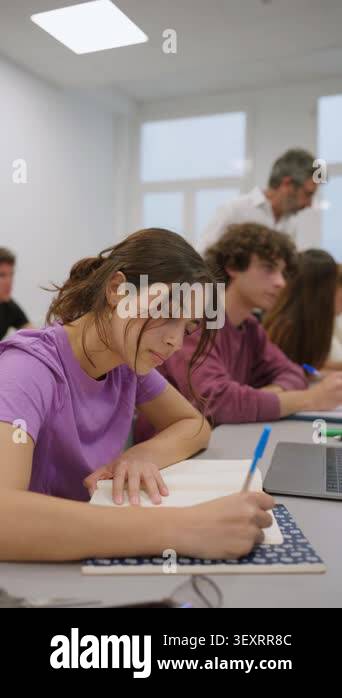Young female student concentrating and writing in a notebook during a ...