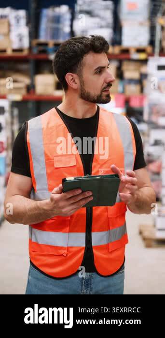 Male warehouse manager in a safety vest using a digital tablet to check ...