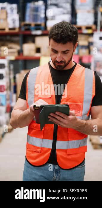 Male worker wearing an orange safety vest, using a tablet for inventory ...