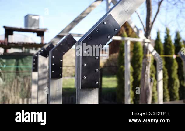 Close up shows wooden posts joined by black connector plates with bolts ...