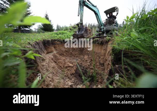Turquoise mini excavator digs and lifts clay from a deep pit as earth ...