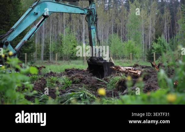 Turquoise excavator bucket digs turf, lifts sod and roots as soil falls ...