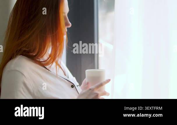 Beautiful young redhead woman holding a cup of coffee and enjoying warm ...